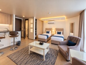 Quarto de hotel moderno com duas camas, área de estar, cozinha compacta e banheiro.