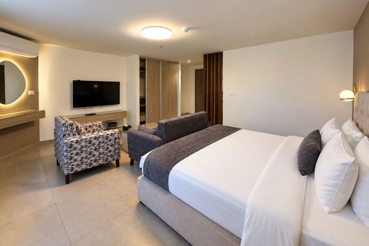 Quarto de hotel com cama grande, televisão, área de estar e closet espaçoso.