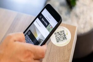 Um smartphone mostra a interface de um aplicativo de hotel com um código QR sobre uma superfície de madeira.