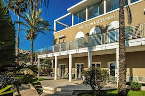 Um hotel com uma placa com o nome 'NAUTILUS EXCELSIOR' na fachada, com estilo arquitetônico moderno, apresentando uma varanda e área de entrada coberta.
