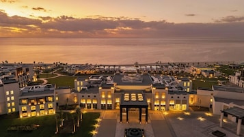 Um resort com vários edifícios, um pátio central e vista para o oceano ao pôr do sol.