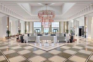 Um hall espaçoso com uma recepção central, grandes janelas e um lustre decorativo.