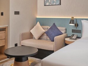 Quarto de hotel com cama, sofá, mesa pequena, abajur e telefone.