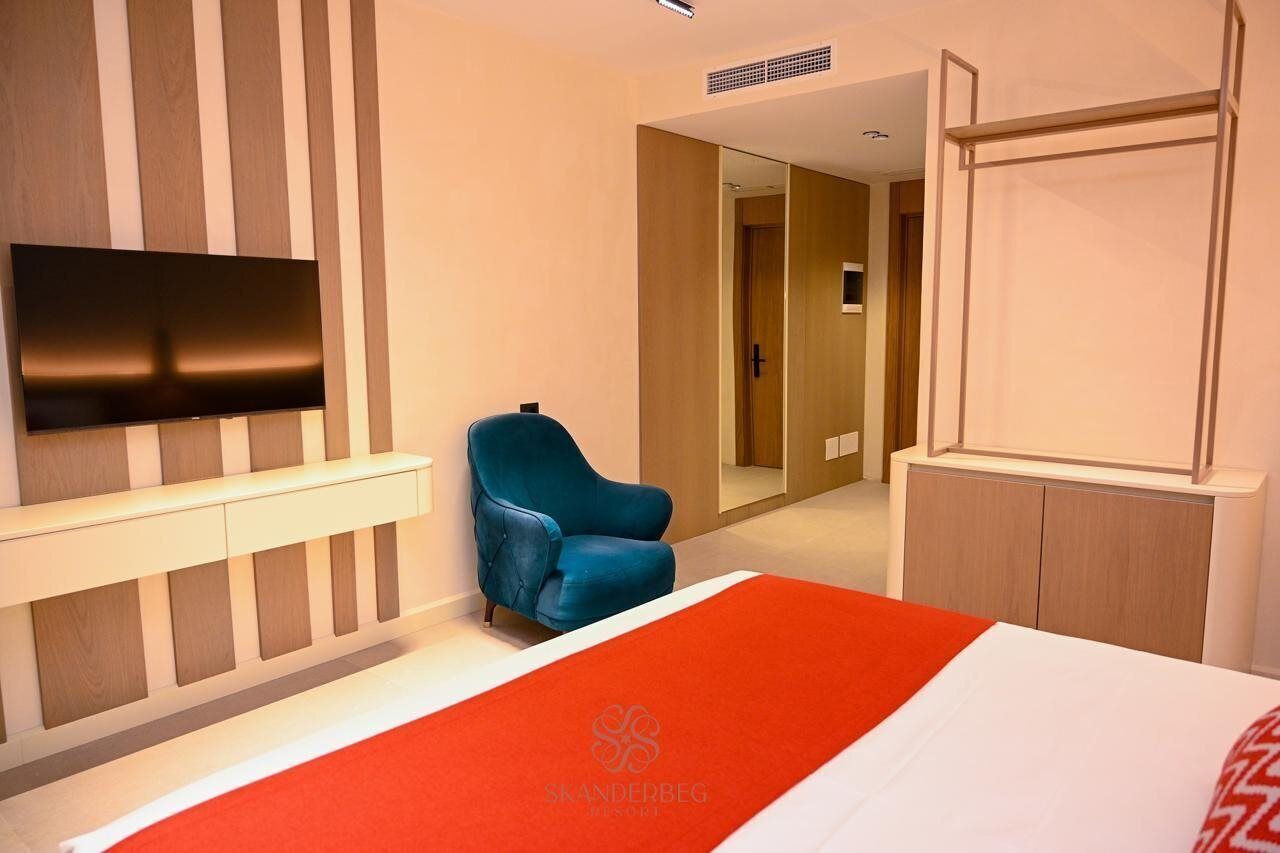 Quarto de hotel com cama, televisão de tela plana na parede, uma cadeira azul e um guarda-roupa.