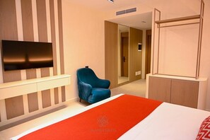 Quarto de hotel com cama, televisão de tela plana na parede, uma cadeira azul e um guarda-roupa.