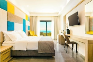 Quarto de hotel com cama, escrivaninha, cadeira, televisão e uma grande janela com vista.