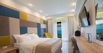 Quarto de hotel com cama, escrivaninha, cadeira e televisão.
