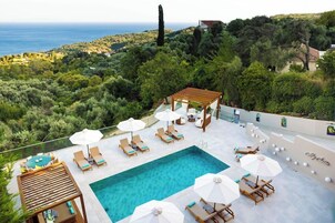 Área de piscina no terraço com espreguiçadeiras e guarda-sóis, cercada por vegetação e com vista para a paisagem costeira.