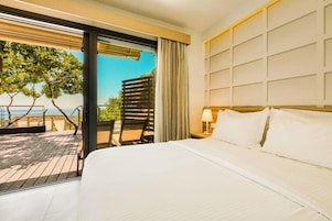 Quarto de hotel com cama, mesa de cabeceira, luminária, janela com vista para árvores e uma varanda.