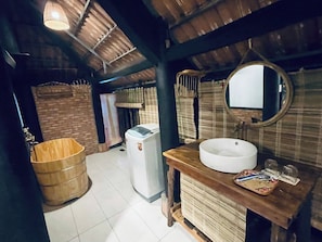 Uma casa de banho rústica com toucador de madeira, um lavatório redondo e um espelho grande.