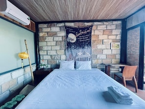 Quarto com cama, mesa de cabeceira, cadeira, mesa, tapeçaria e janela.