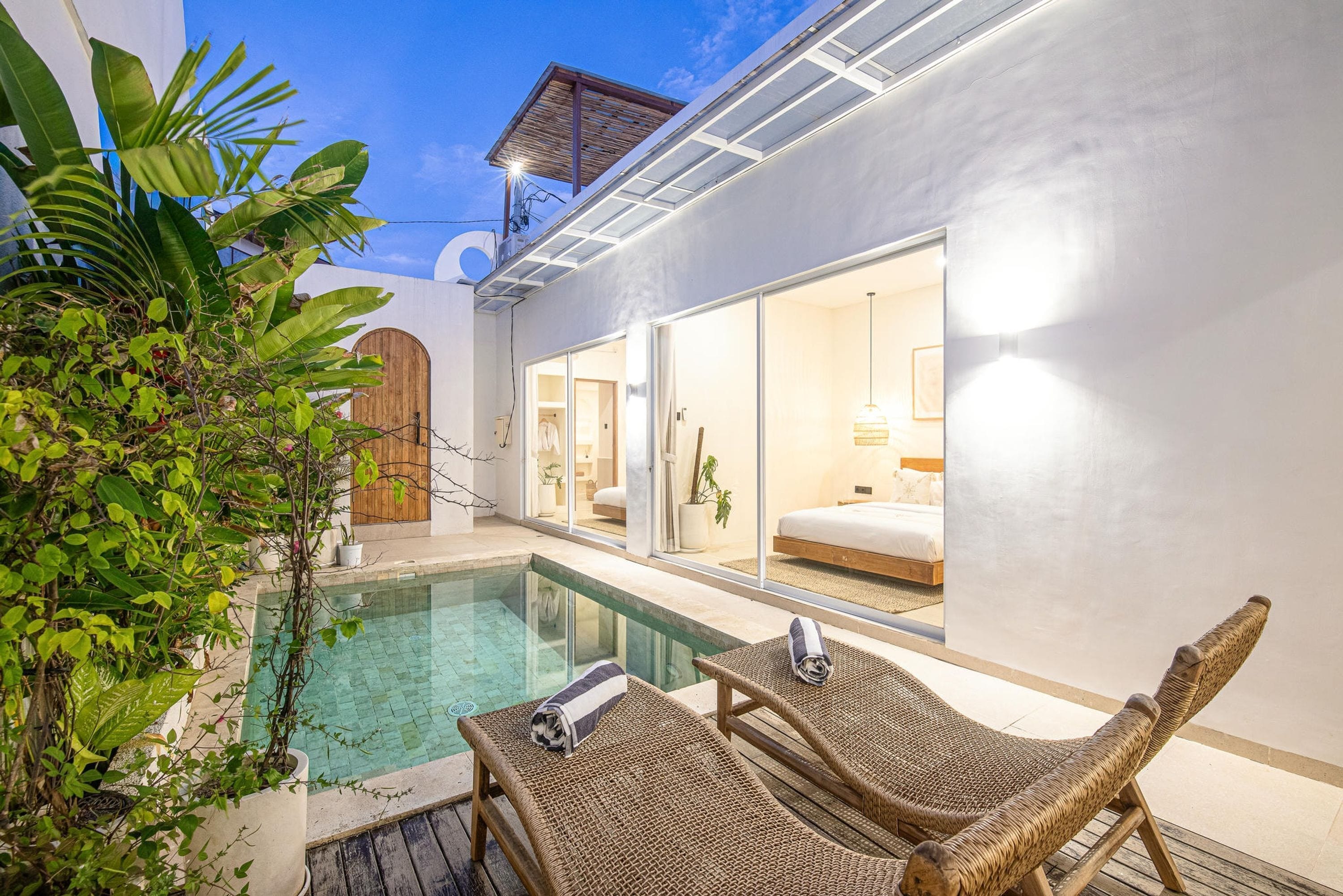 Uma área de piscina moderna ao ar livre, com espreguiçadeiras e um quarto com paredes de vidro.