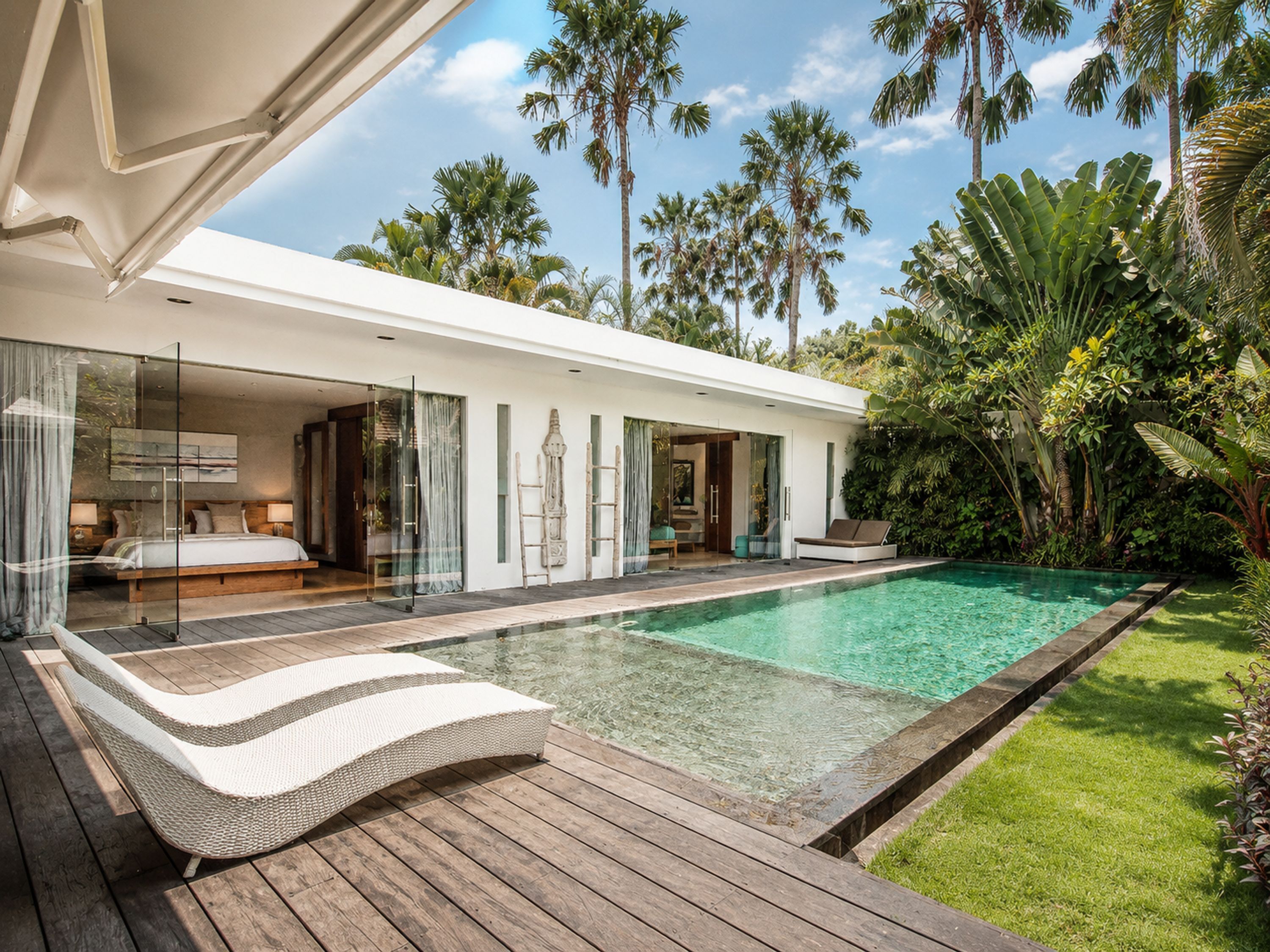 Uma casa moderna com quarto envidraçado, piscina e vegetação tropical exuberante.