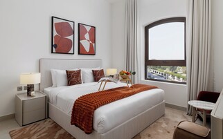 Quarto de hotel com uma cama grande, duas mesas de cabeceira, uma escrivaninha, uma cadeira, uma janela com cortinas e arte abstrata nas paredes.