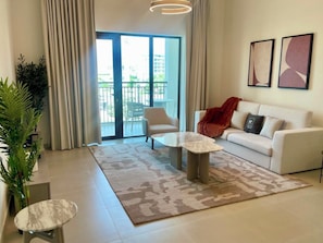 Sala de estar moderna com sofá branco, duas mesas de centro, tapete estampado e varanda com vista.