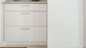Um guarda-roupa branco com um quadro emoldurado, um vaso azul-esverdeado e uma tigela numa bancada.
