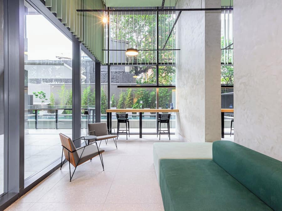 Um interior moderno com um sofá verde, uma área de jantar com mesa e cadeiras, e janelas amplas com vista para o verde.