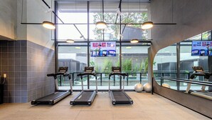 Academia com esteiras, bolas de exercício e uma TV exibindo um anúncio.