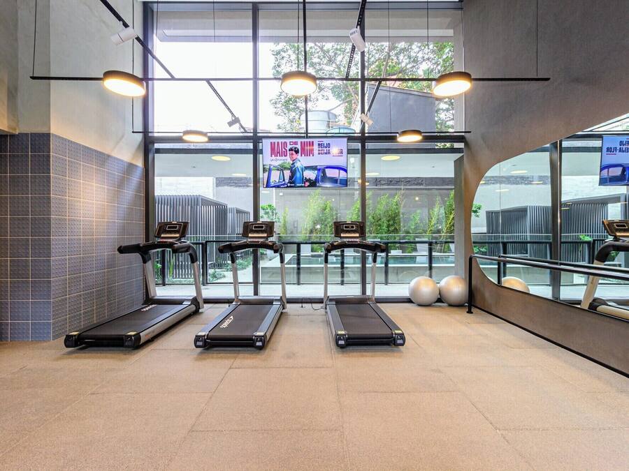 Academia com esteiras, bolas de exercício e uma TV exibindo um anúncio.