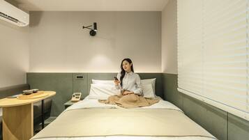 Quarto de hotel com uma cama, mesa de cabeceira e uma luminária na parede.
