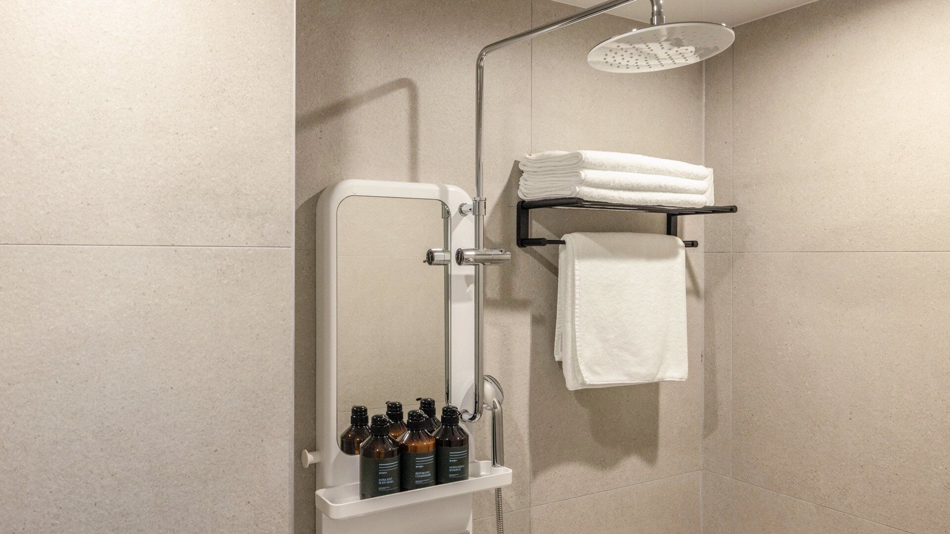 Área de duche com chuveiro manual, um porta-toalhas com uma toalha dobrada e uma prateleira com garrafas de champô e condicionador.