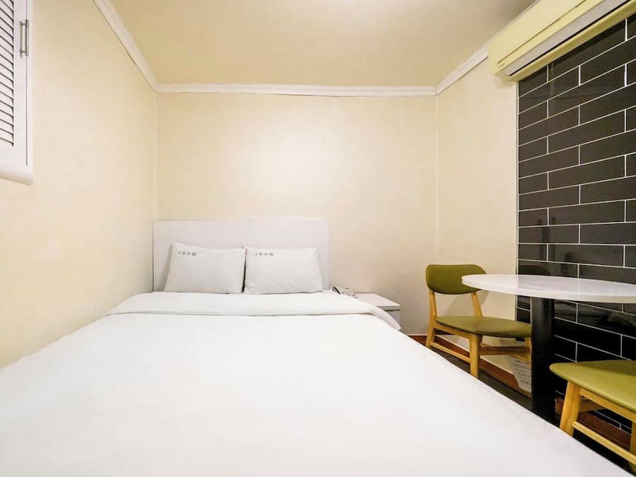 Quarto pequeno com cama de solteiro, uma mesa redonda e duas cadeiras.