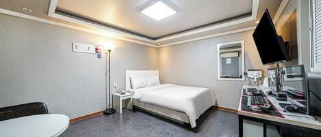 Quarto de hotel com cama, escrivaninha, cadeira e televisão de tela plana.