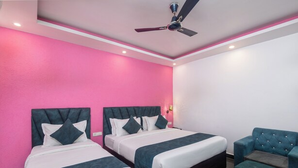 Quarto de hotel com duas camas, ventoinha no teto e um espaço para sentar.