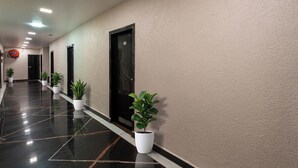 Um corredor com várias portas, plantas em vasos e piso cerâmico.