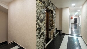 Corredor com parede de mármore e chão em piso preto e branco.