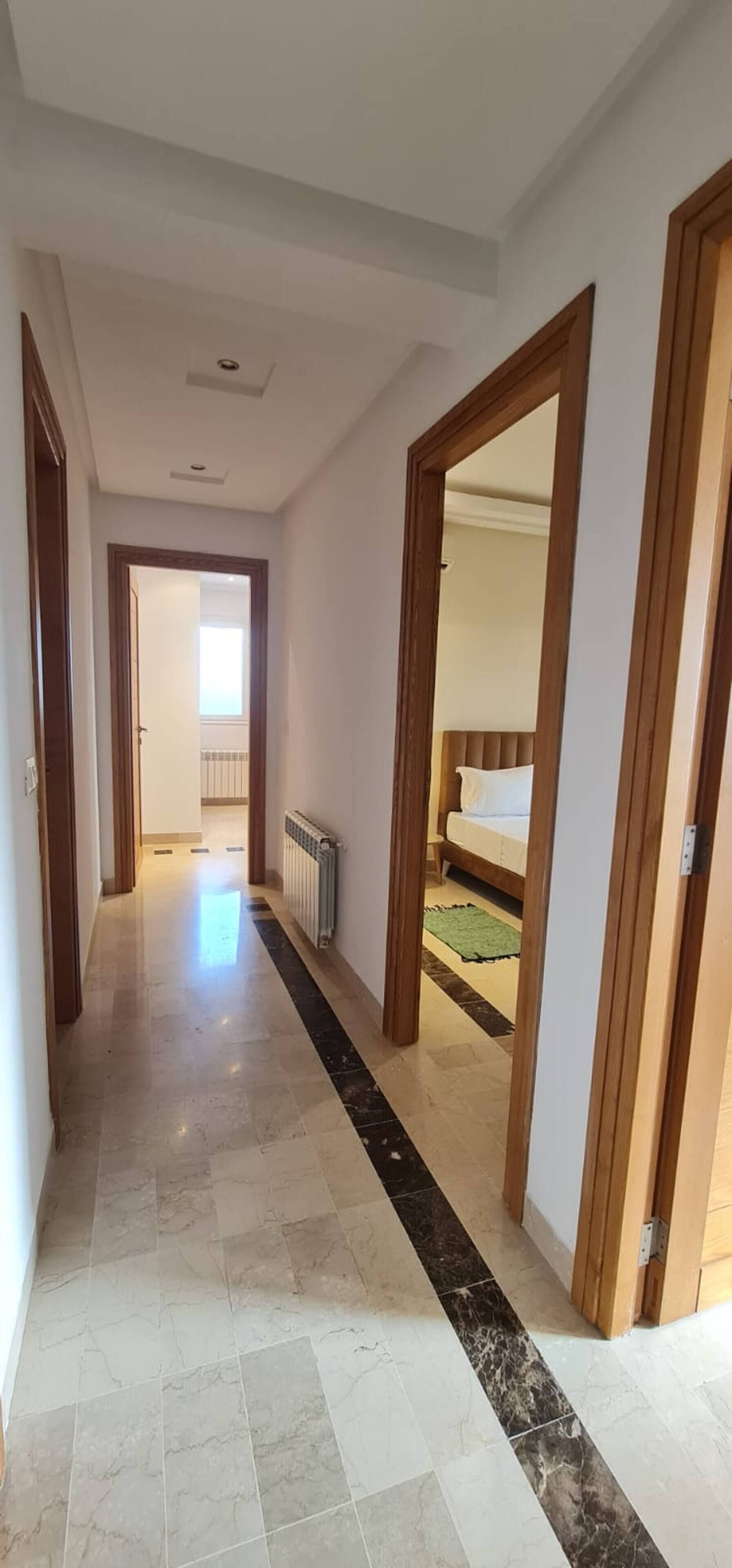 Corredor que leva a um quarto com uma cama, um radiador e uma janela.