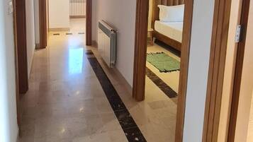 Corredor que leva a um quarto com uma cama, um radiador e uma janela.