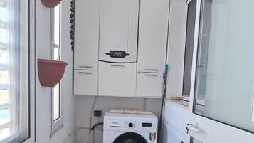 Uma lavanderia com máquina de lavar de abertura frontal, secadora e uma pequena janela.