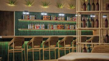 Uma área de bar com várias prateleiras de garrafas, cadeiras de madeira e uma parede revestida de azulejos verdes.