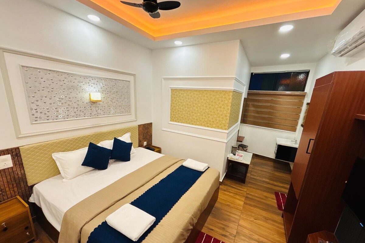 Quarto de hotel com cama, mesas de cabeceira, escrivaninha e televisão.