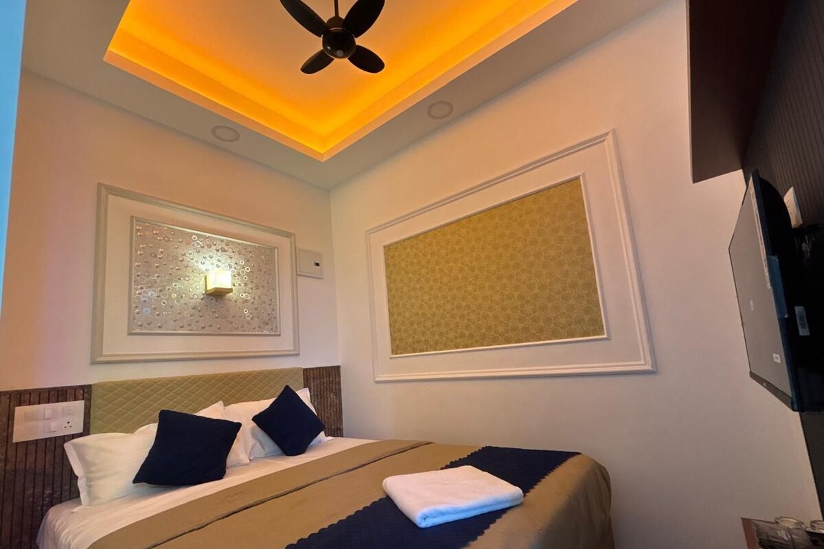 Quarto de hotel com uma cama, ventilador de teto, luminária na parede e televisão.