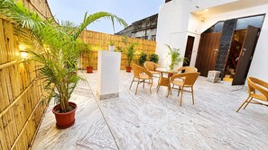 Um pátio moderno ao ar livre com cerca de bambu, plantas em vasos, móveis de vime e piso de azulejos.