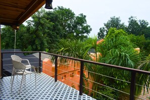 Varanda com piso estampado, uma cadeira e grade, com vista para um jardim com diversas plantas e árvores.