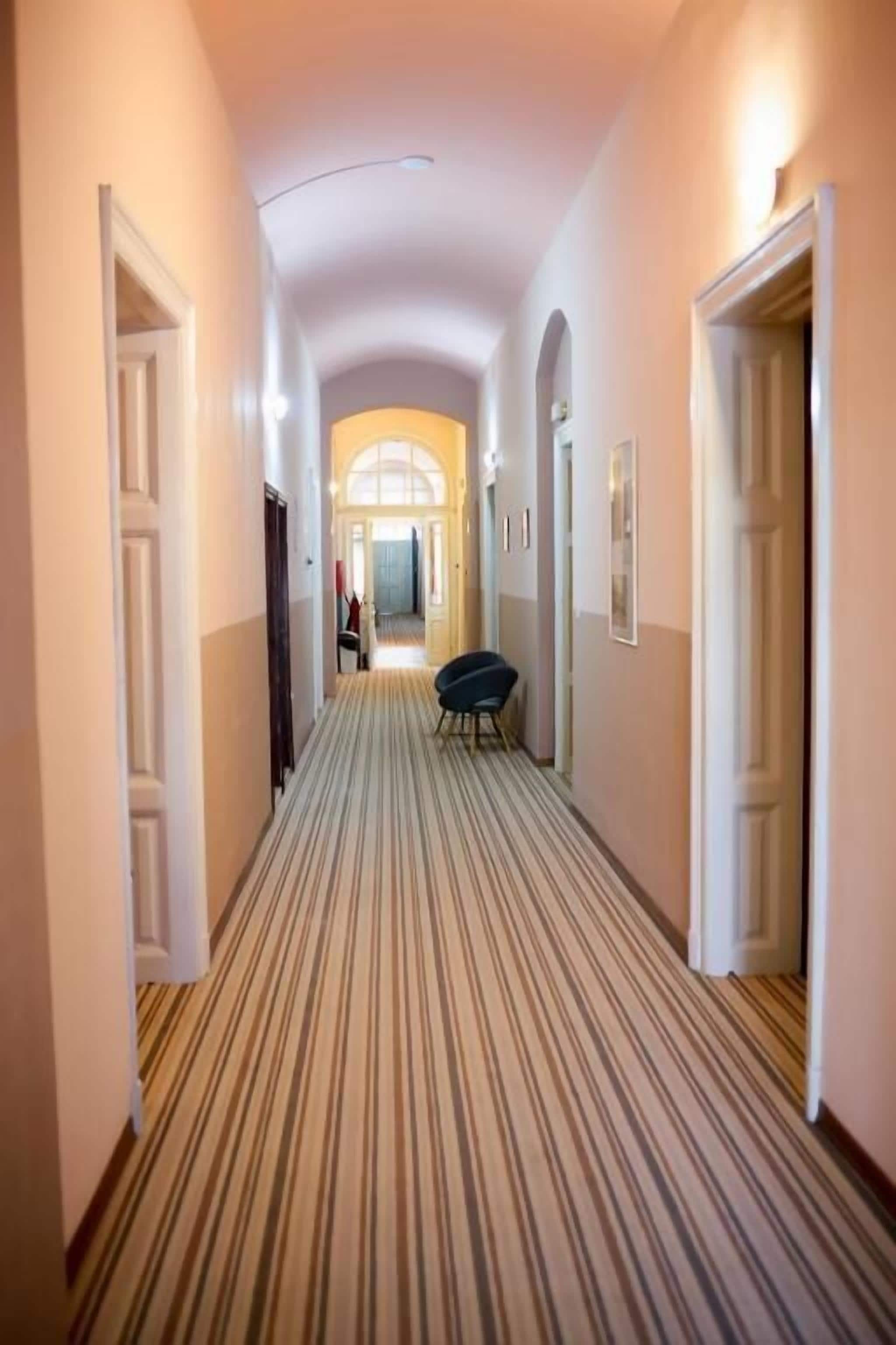 A hotel hallway with a striped carpet, white walls, and doors on either side.