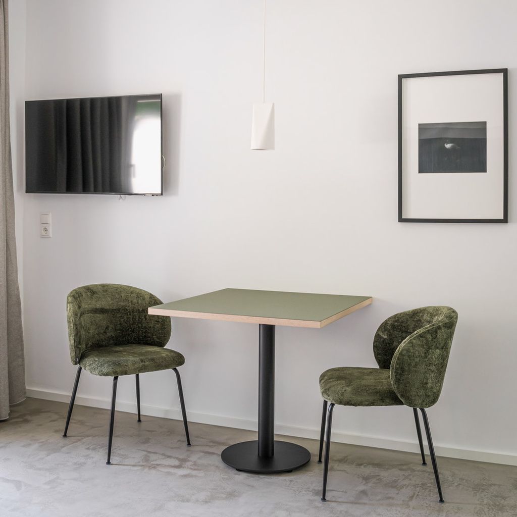 Quarto com uma mesa redonda e duas cadeiras, uma TV de tela plana fixada na parede e um quadro emoldurado.