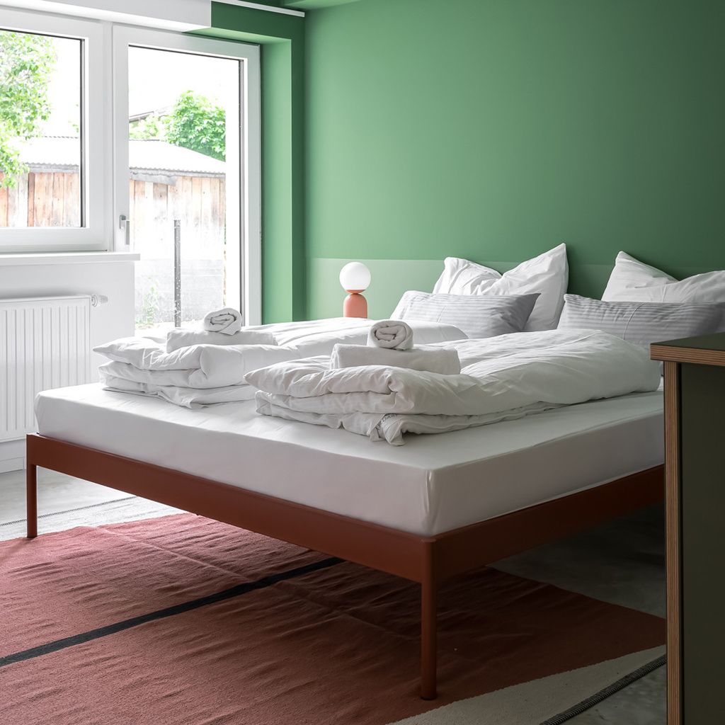 Cama bem arrumada com lençóis e toalhas brancas, cabeceira de madeira e vista para o exterior pela janela.