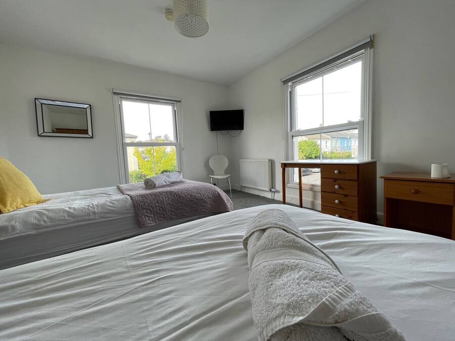 Quarto com duas camas, cômoda, televisão e janela com vista para edifícios e áreas verdes.