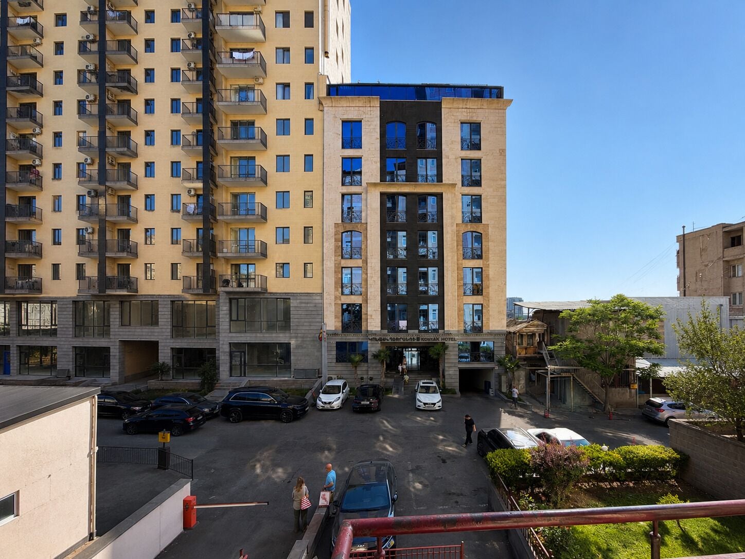 Um hotel de vários andares com um estacionamento à frente, destacando uma construção moderna com varandas e um céu claro.