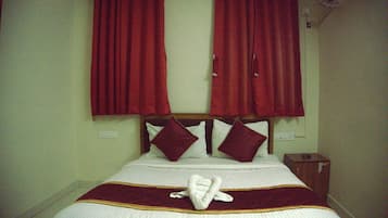 Quarto de hotel com uma cama, cortinas vermelhas, um painel de cabeceira de madeira e uma pequena mesa de cabeceira de madeira.