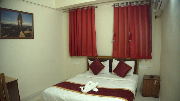 A hotel room with a bed, red curtains, a painting on the wall, and a wooden nightstand.