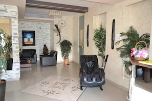 Ampla sala de estar com sofá de couro preto, poltrona de massagem e uma grande planta em vaso.