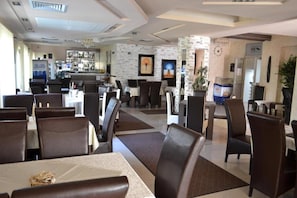 Uma área de refeições de hotel com mesas, cadeiras, um bar e um balcão de recepção.