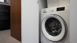 Uma máquina de lavar Whirlpool com painel de controle, num quarto com porta de madeira e soalho em azulejos.