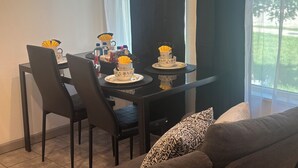 Uma área de refeições com mesa posta para quatro pessoas, cadeiras, um sofá e vista para o verde lá fora.