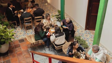 Uma sala de jantar com várias mesas e cadeiras, cercada por plantas em vasos e um piso com padrão.